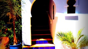 Escadaria que leva a um interior escuro, ladeada por plantas em vasos e uma parede com um olho de chave.