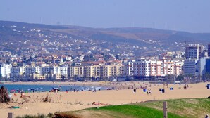 Paisagem costeira com praia, edifícios e turbinas eólicas ao fundo.
