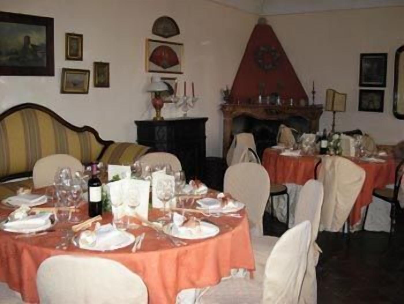 Uma sala de jantar com uma mesa redonda posta para refeição, lareira e quadros nas paredes.