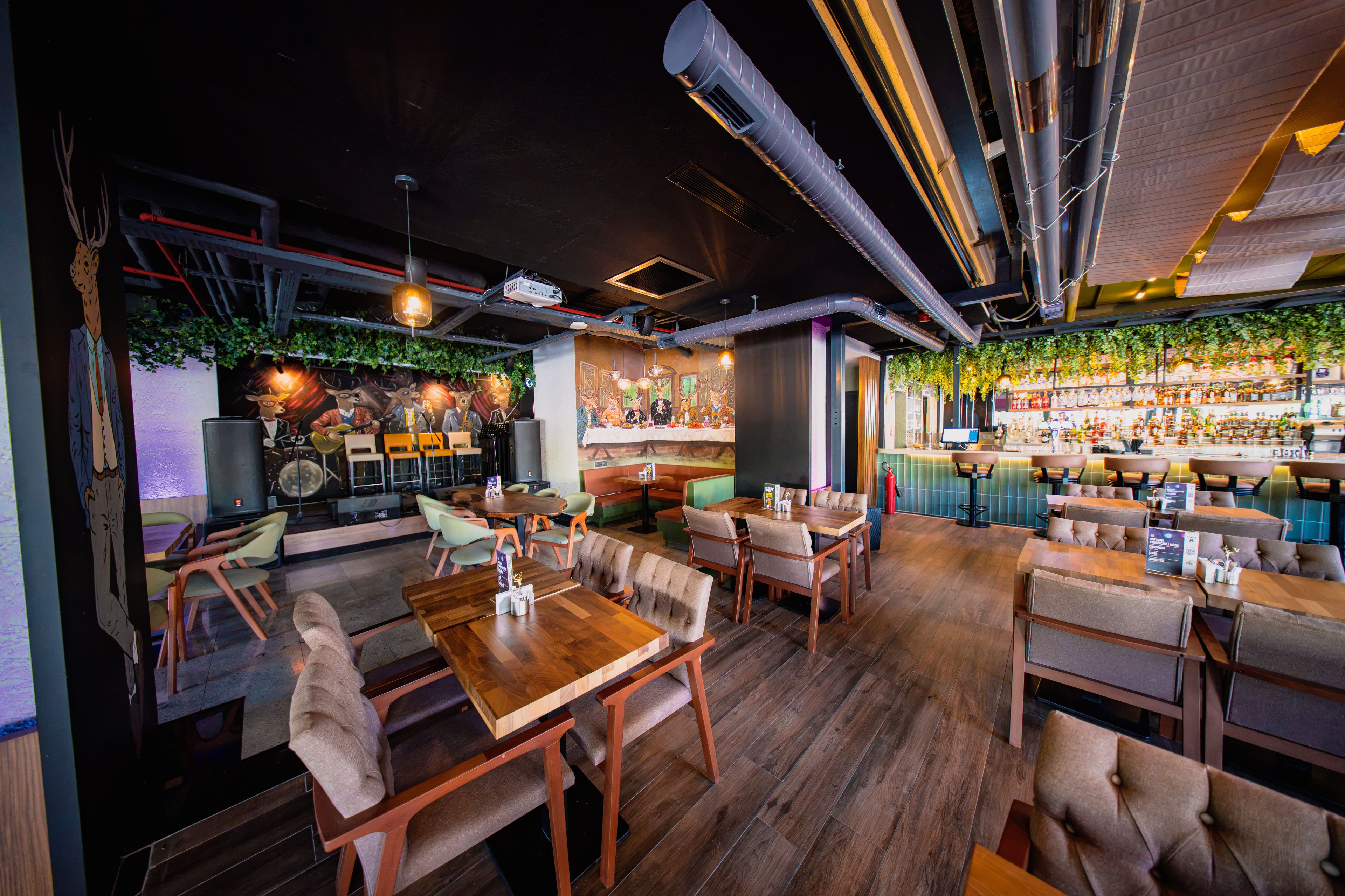 Interior de restaurante com mesas e cadeiras de madeira, área de bar com banquetas e um mural na parede.