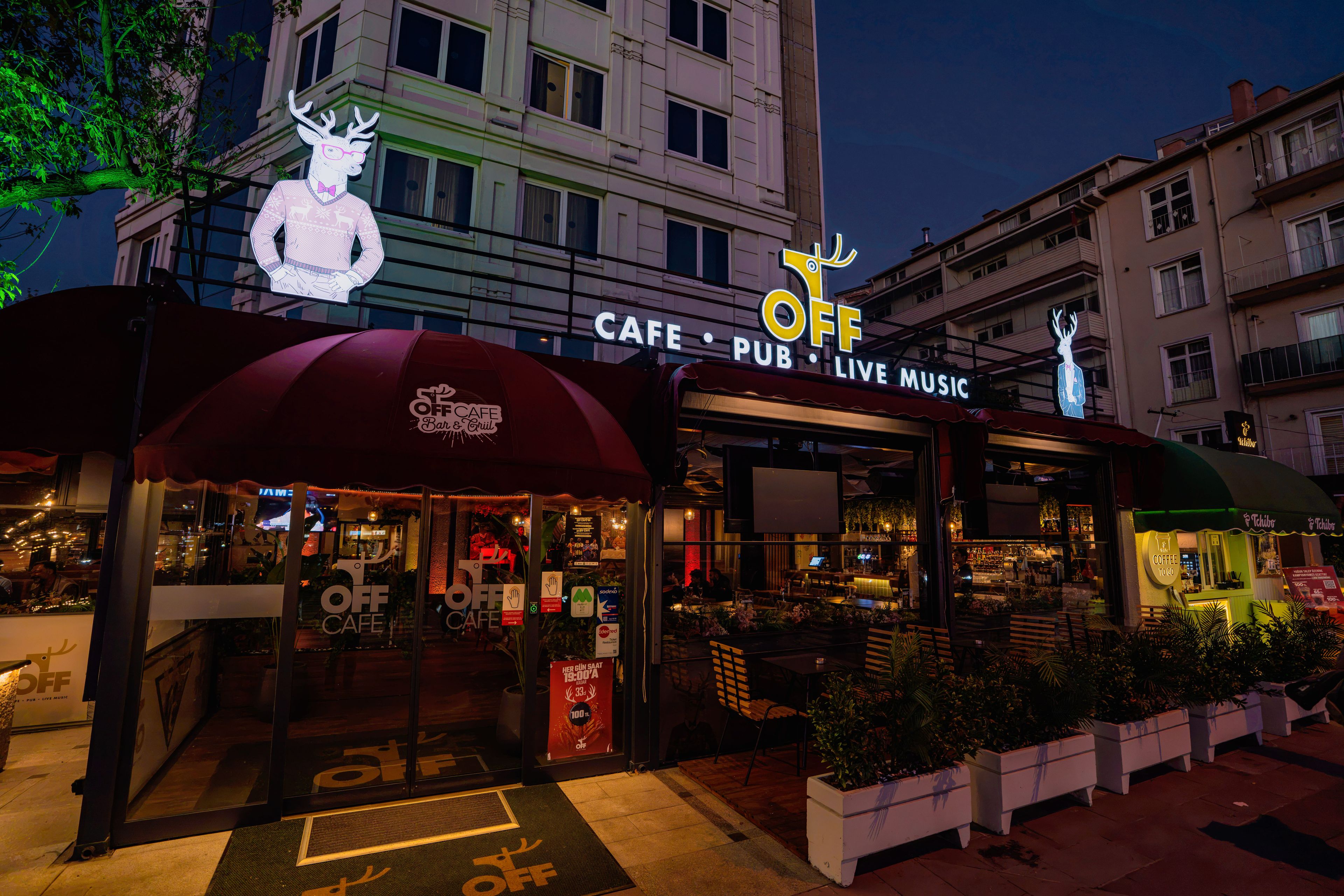 Café com placa de música ao vivo, mesas ao ar livre e decoração de cabeça de veado.