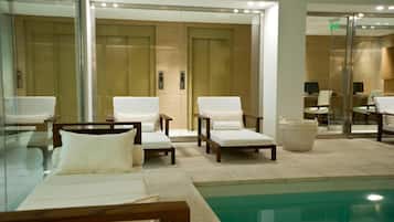 Um hall de hotel com piscina, espreguiçadeiras e um elevador.