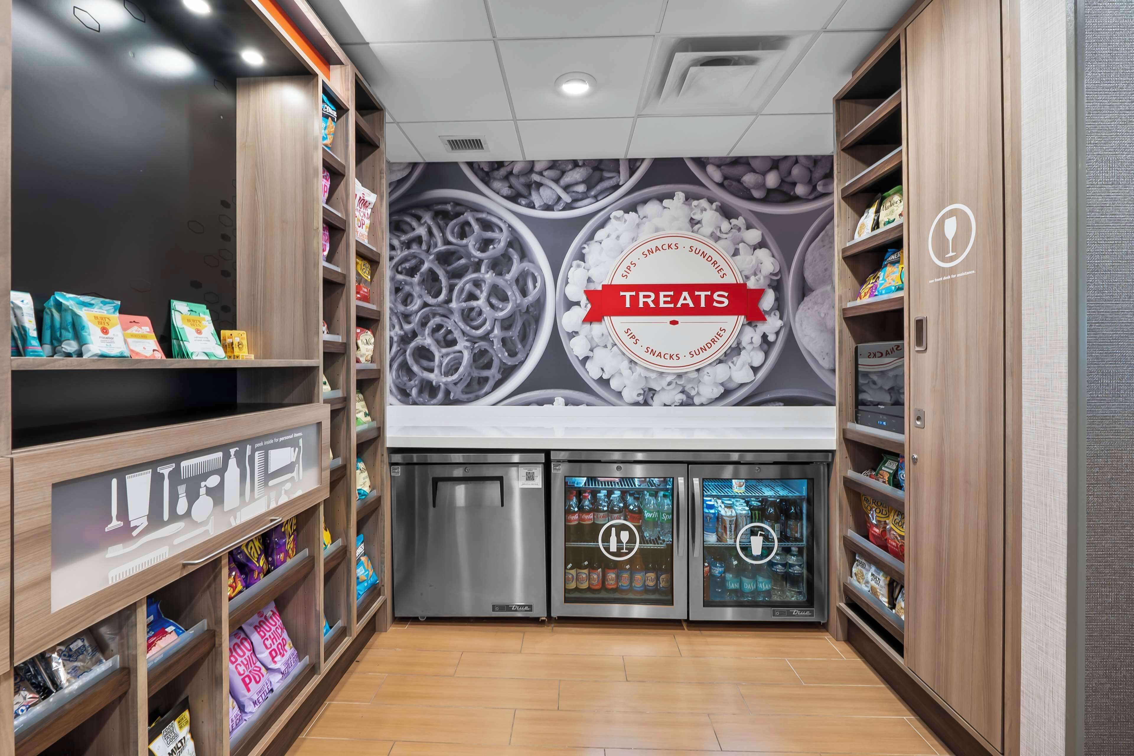 Quiosque de lanches e bebidas com seções refrigeradas e prateleiras cheias de diversos petiscos e bebidas.
