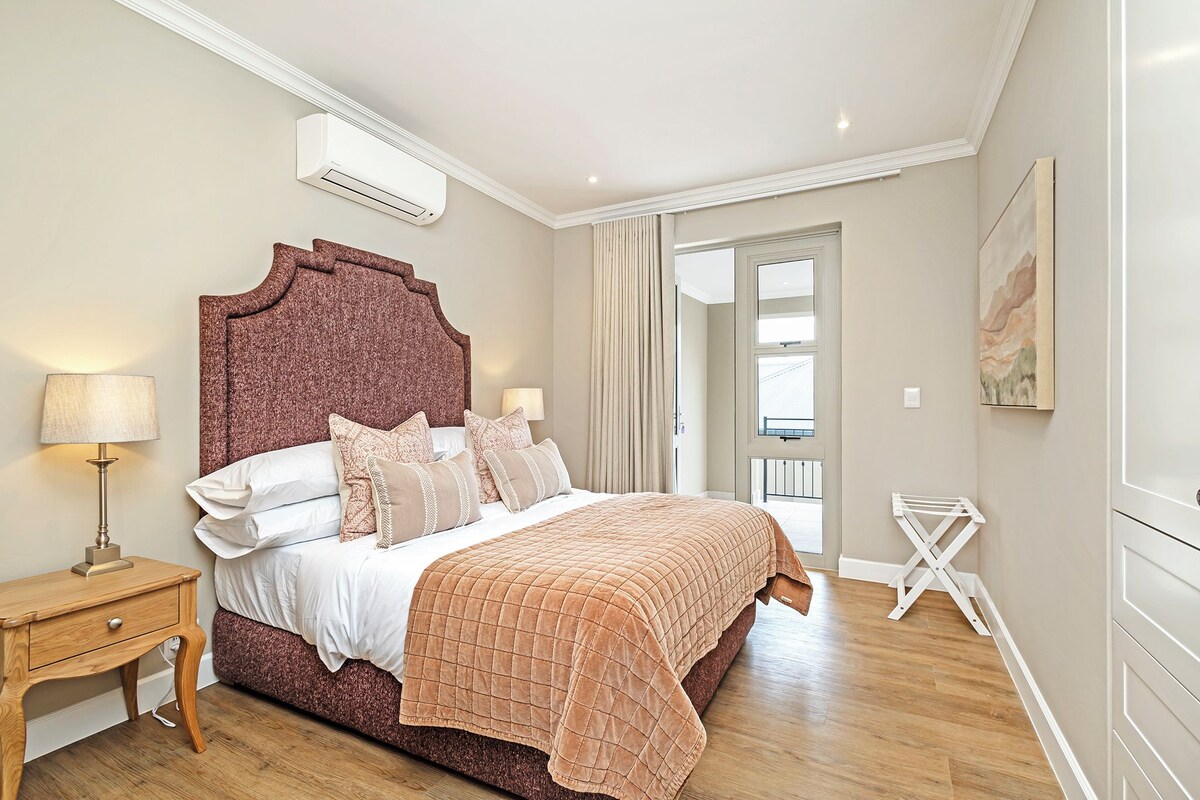 Um quarto com uma cama, abajures, mesa de cabeceira, uma janela e um quadro na parede.
