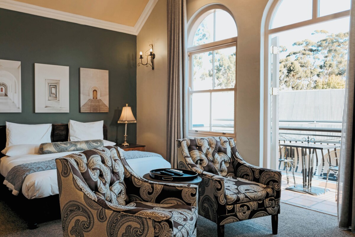 Quarto de hotel com cama, duas cadeiras, uma mesa e obras de arte na parede.