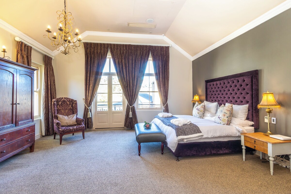 Quarto com cama grande, cadeira, penteadeira e lustre.