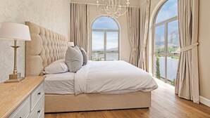 Quarto com uma cama grande, um candelabro, uma cômoda e vista para um lago.