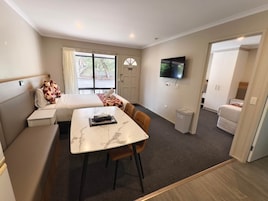 Quarto de hotel compacto com cama, uma pequena mesa com cadeiras, televisão e guarda-roupa.