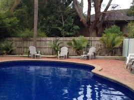 Piscina com borda de tijolos e cadeiras brancas ao redor.