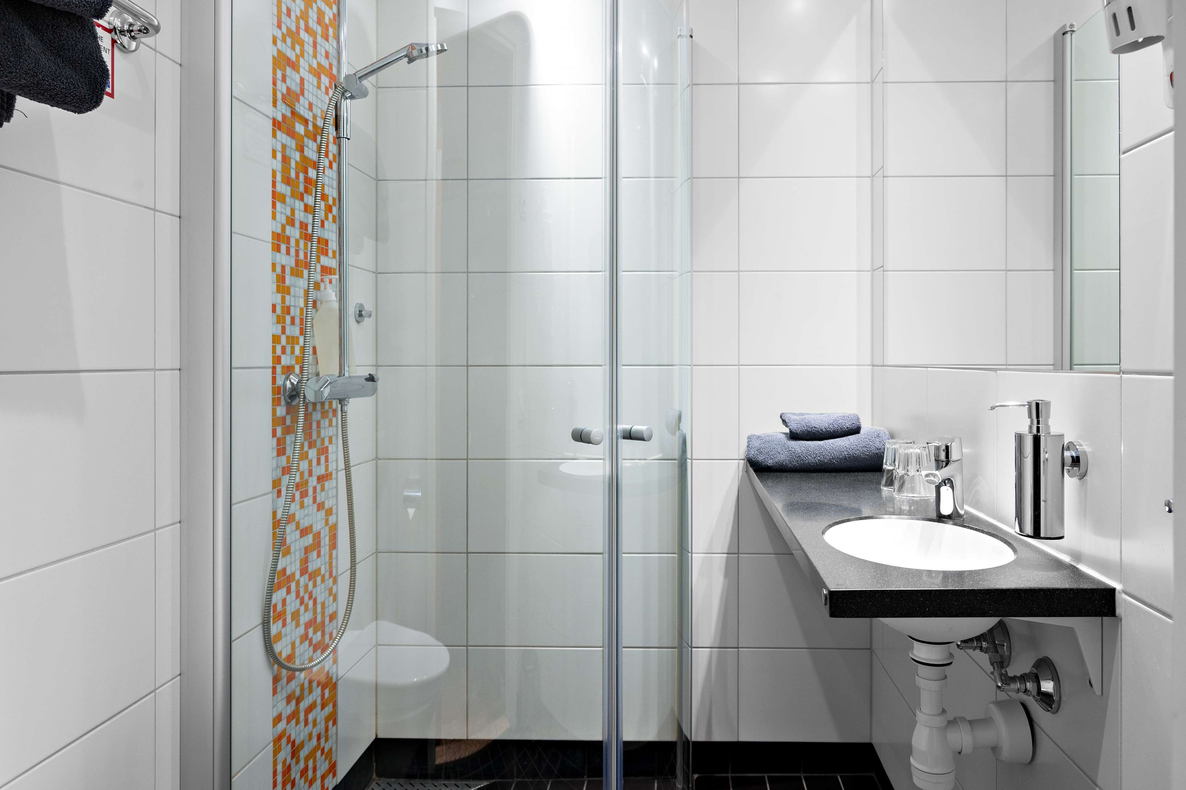 Casa de banho moderna com cabine de duche em vidro, lavatório branco e painel de azulejos.