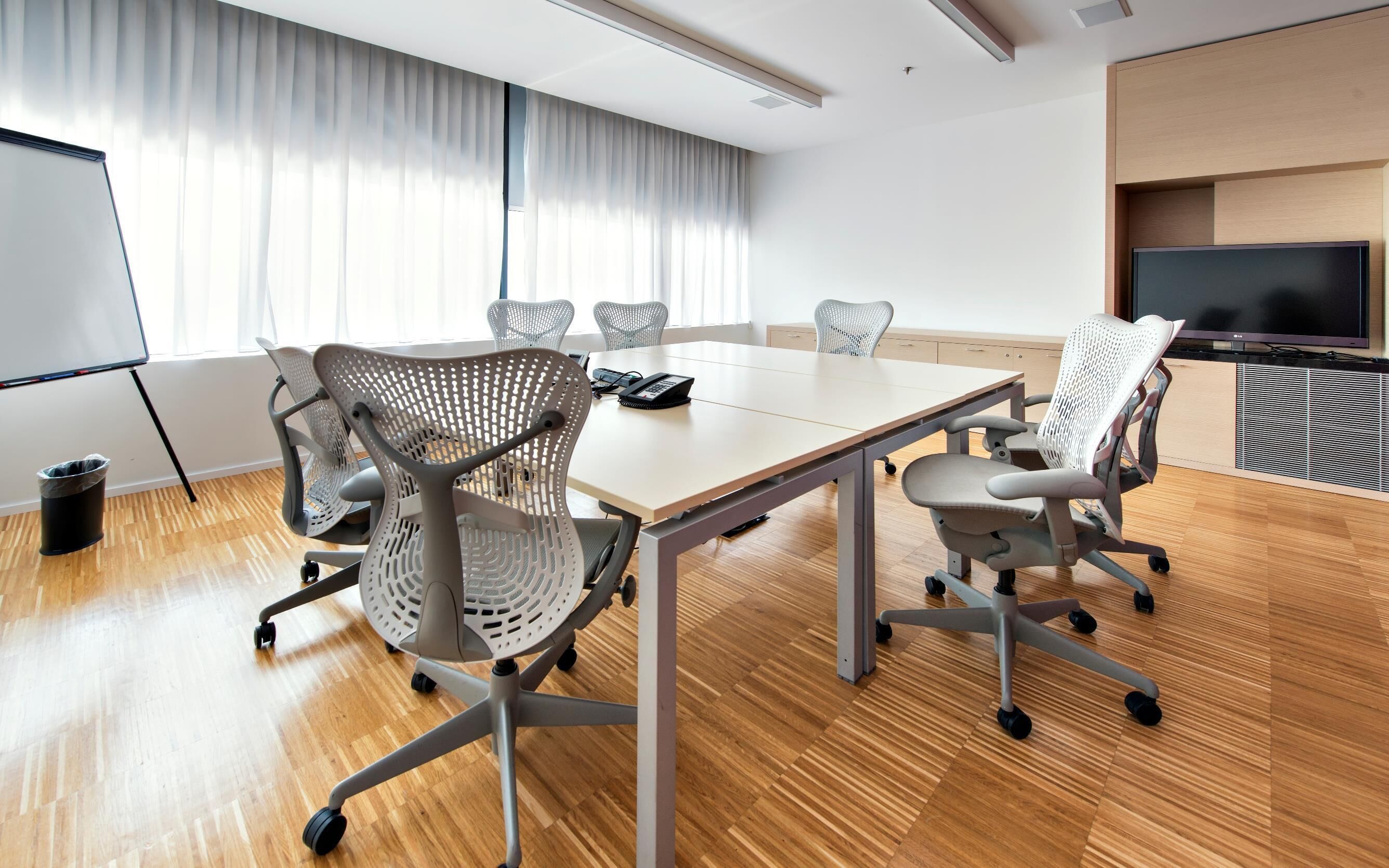 Uma sala de conferências com uma mesa comprida, várias cadeiras, um quadro branco e uma televisão.