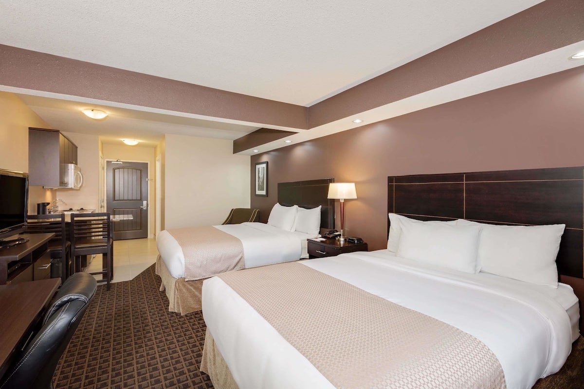 Quarto de hotel com duas camas, uma escrivaninha, uma cadeira, uma televisão e um abajur.