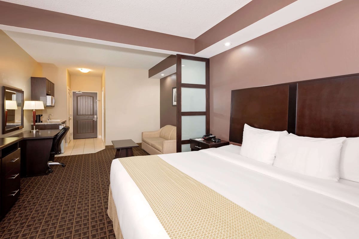 Quarto de hotel com uma cama grande, uma escrivaninha com cadeira, uma mesa pequena, um abajur e um espelho.