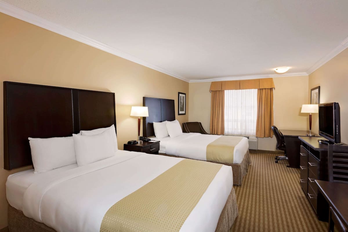 Quarto de hotel com duas camas, uma escrivaninha, televisão e janela com cortinas.
