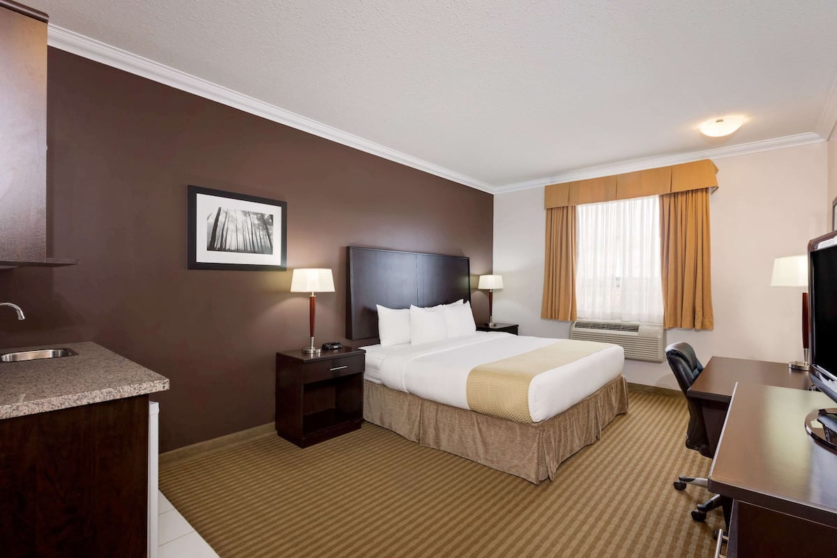 Quarto de hotel com cama, escrivaninha, cadeira e pequena área de cozinha.