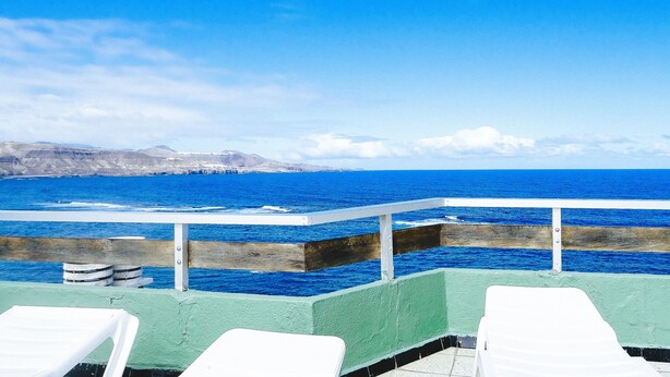 Vista para o mar, com grade e cadeiras de lounge brancas.