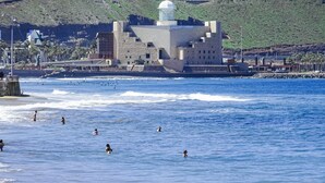 Um edifício costeiro com cúpula, rodeado por uma linha costeira rochosa e ondas.