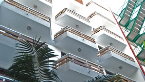 Um edifício de vários andares com varandas, uma palmeira e uma planta em primeiro plano.