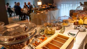 Buffet com diversos alimentos e um grupo de pessoas ao fundo.