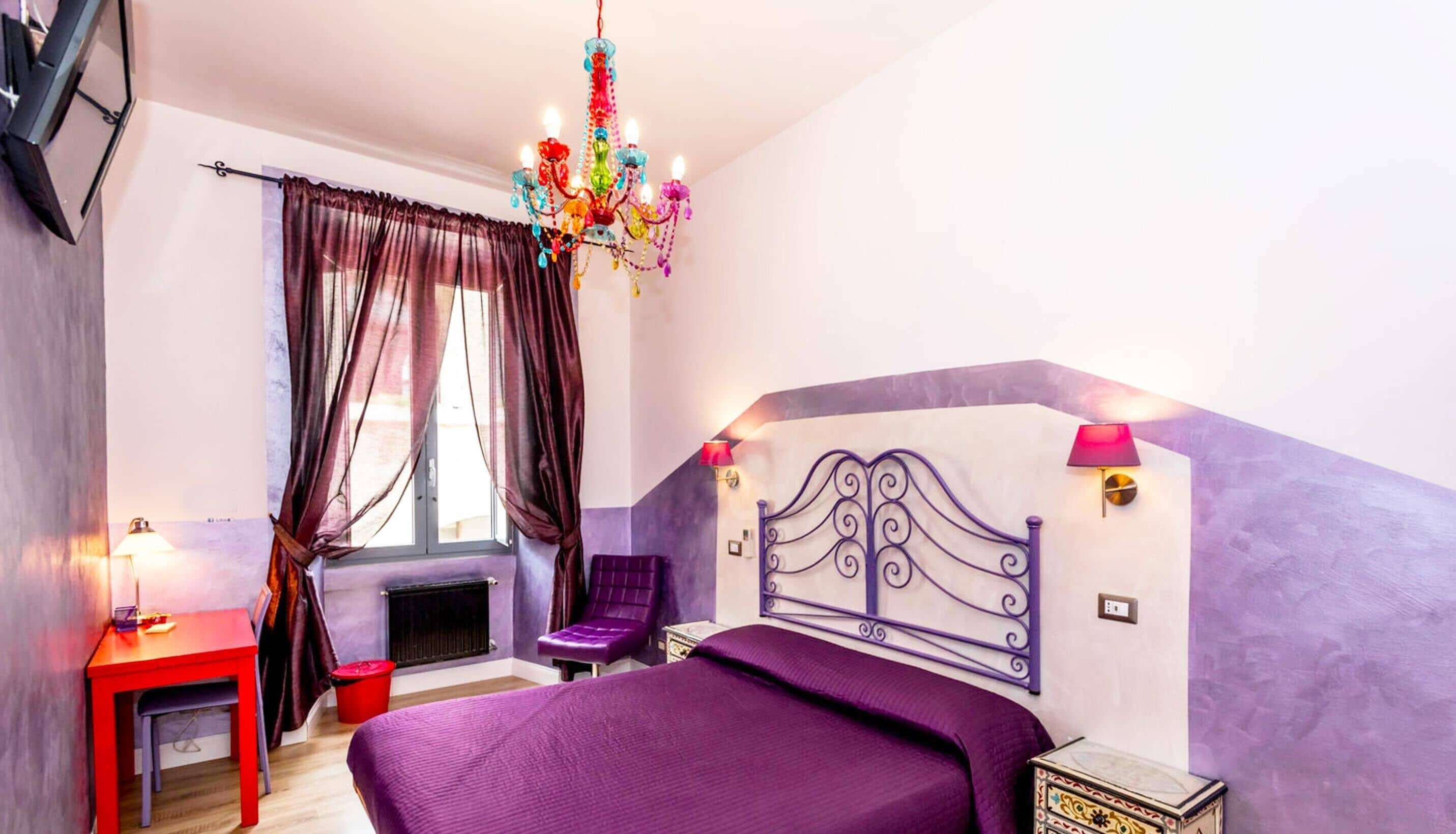 Quarto com cama roxa, um candelabro, uma cadeira e uma pequena mesa.