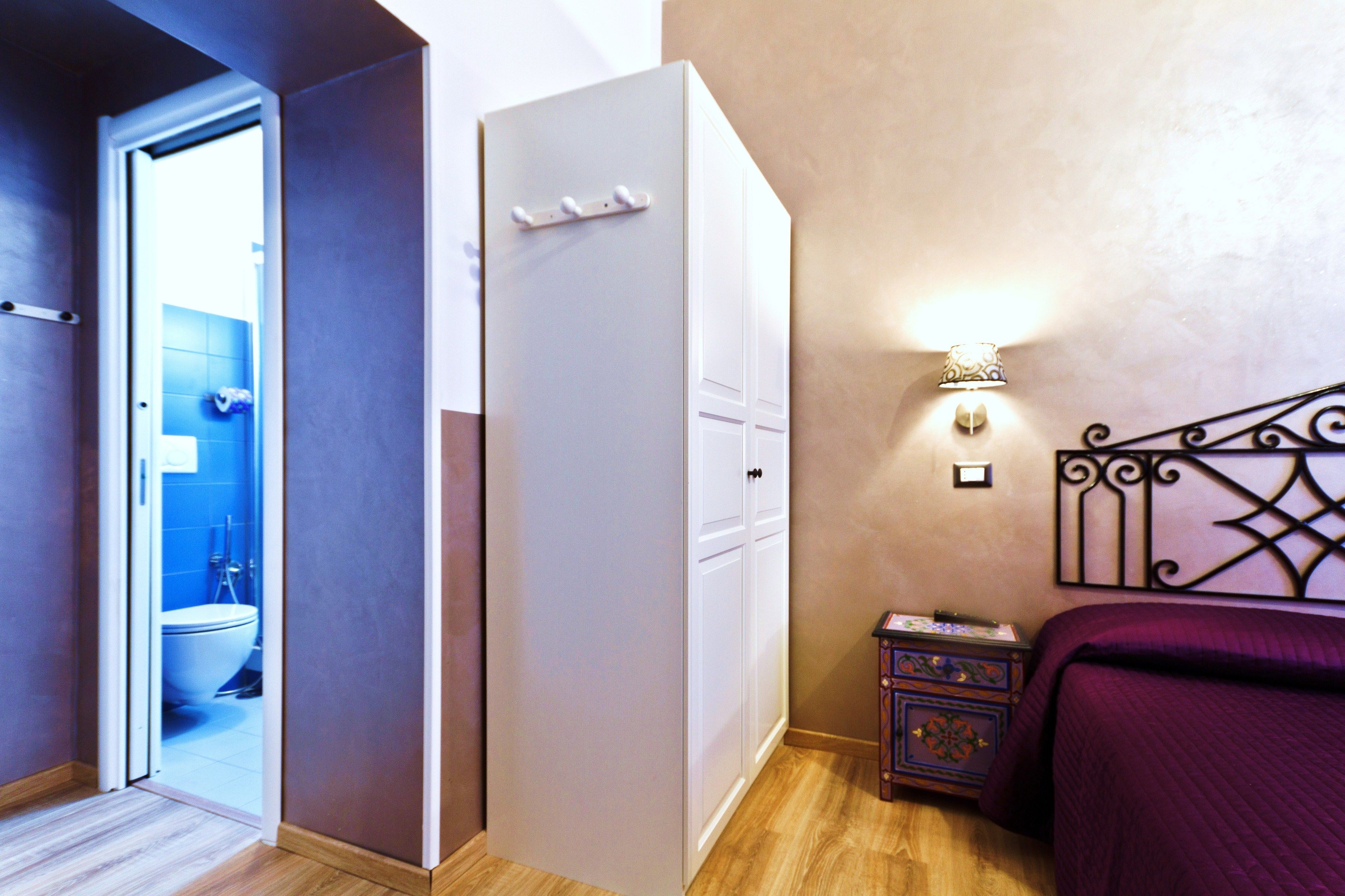 Quarto com cama, guarda-roupa, mesa de cabeceira e luminária na parede.