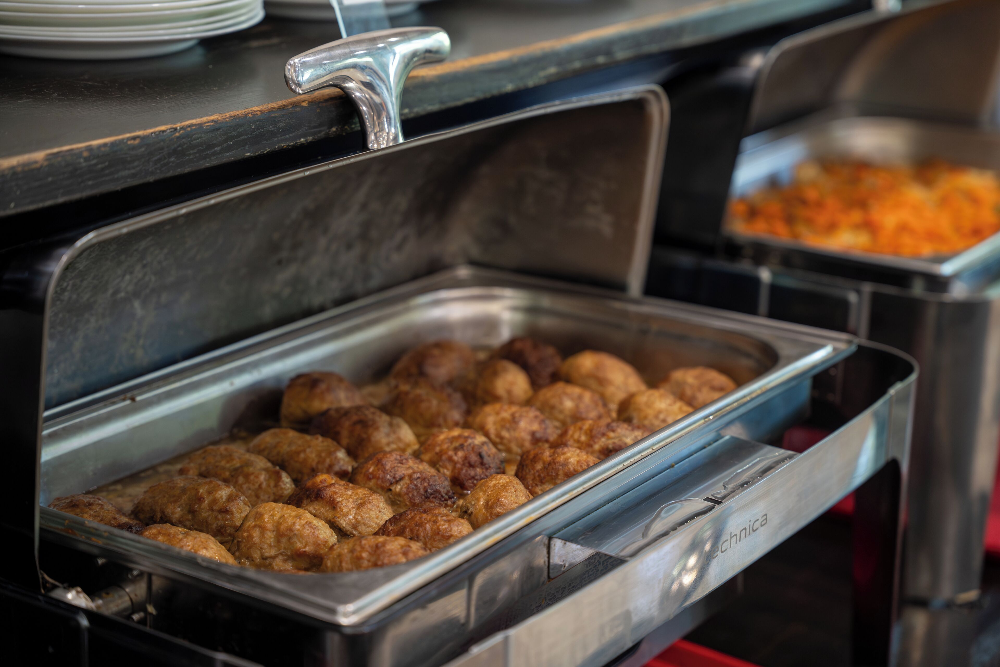 Buffet com um prato de almôndegas e um recipiente que parece ser um assado.