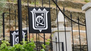 Um portão com um logotipo, uma parede de pedra e bandeiras ao fundo.
