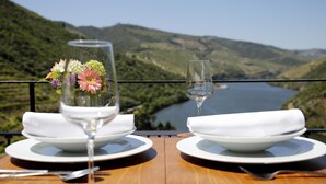 Uma mesa posta com pratos, copos e um vaso de flores, com vista para um vale deslumbrante.