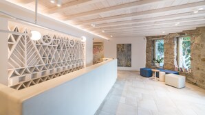 Uma área de recepção moderna com design geométrico na parede, parede de pedra com janelas e um espaço de estar com mesa redonda e bancos acolchoados.