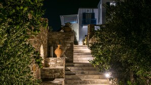 Uma escadaria de pedra leva a um edifício branco com persianas azuis, rodeado por vegetação.
