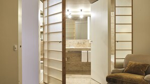 Quarto com cama, sofá, guarda-roupa de madeira e banheiro com pia e espelho.