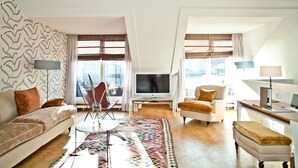 Uma sala de estar moderna com um sofá, poltrona, televisão e uma escrivaninha com computador.