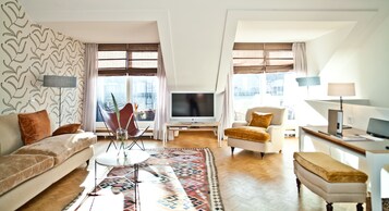 Uma sala de estar moderna com um sofá, poltrona, televisão e uma escrivaninha com computador.