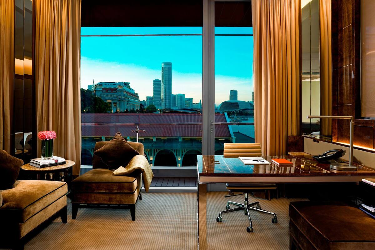 Quarto de hotel com uma janela grande, uma escrivaninha, uma cadeira e um sofá.