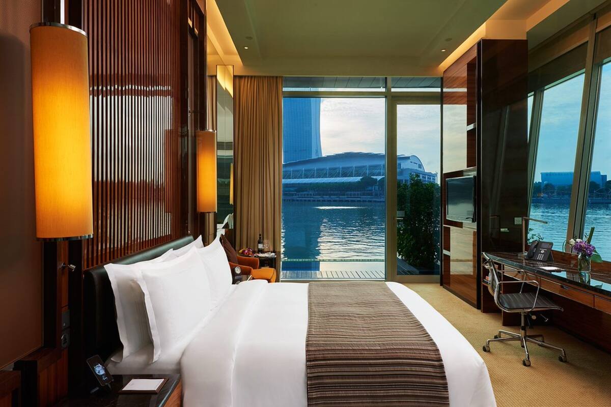 Quarto de hotel com uma cama grande, uma escrivaninha, uma cadeira e vista para a água e uma ponte.