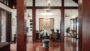 Um hall de hotel com vigas de madeira, um balcão de recepção, um candelabro e um vaso grande cheio de flores.