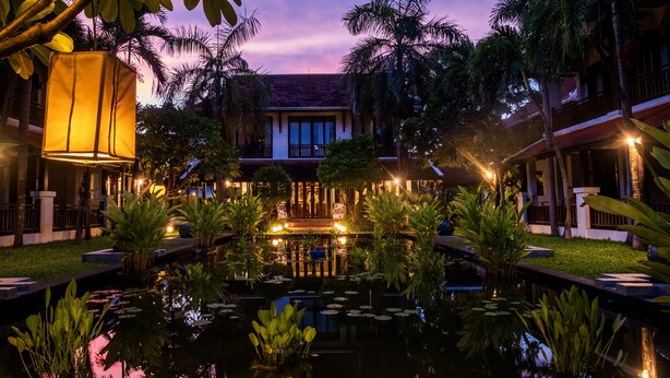 Um resort com piscina, palmeiras e um edifício com grandes janelas.