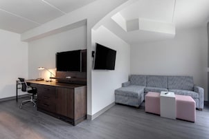 Quarto moderno com escrivaninha, cadeira, duas camas e televisão.