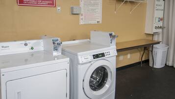 Uma área de lavanderia com duas máquinas de lavar Whirlpool, um quadro de segurança e um dosador de sabão.