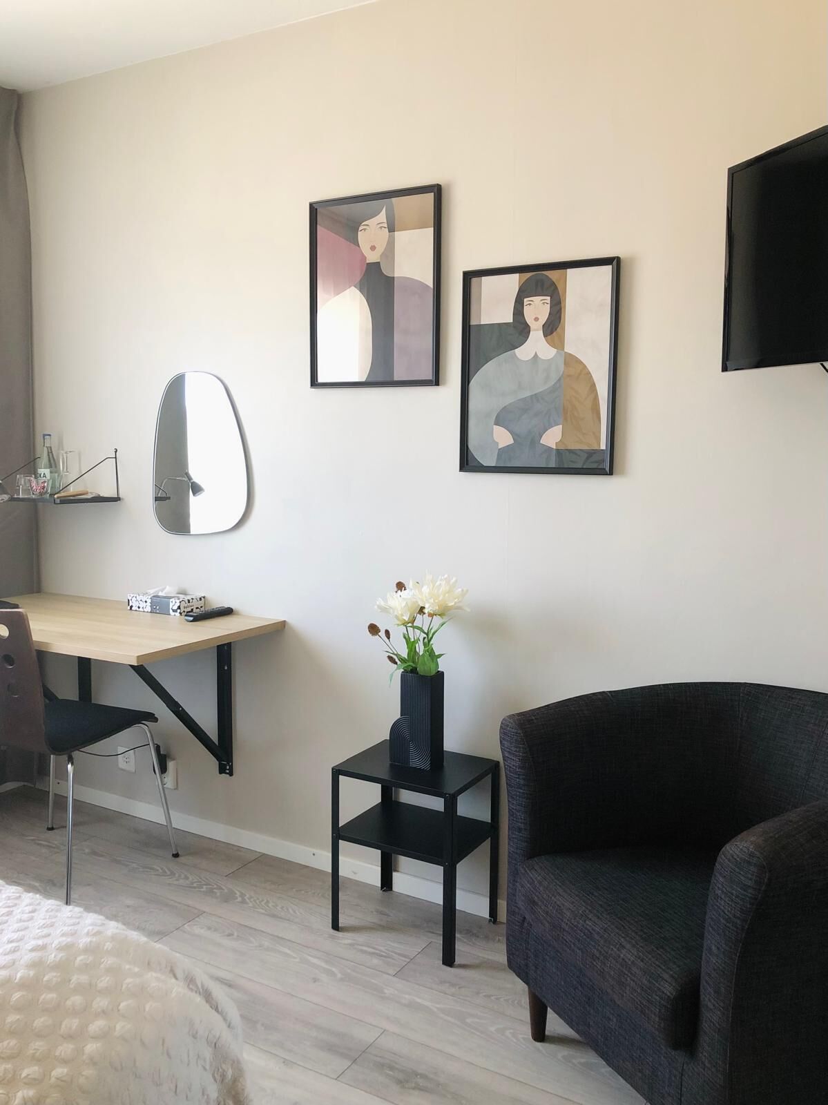 Uma sala de estar moderna com uma escrivaninha, uma cadeira, uma pequena mesa lateral com um vaso de flores e duas obras de arte emolduradas na parede.