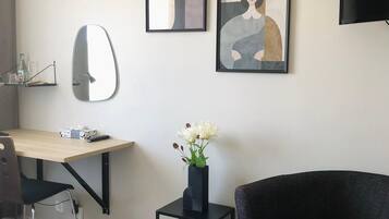 Uma sala de estar moderna com uma escrivaninha, uma cadeira, uma pequena mesa lateral com um vaso de flores e duas obras de arte emolduradas na parede.