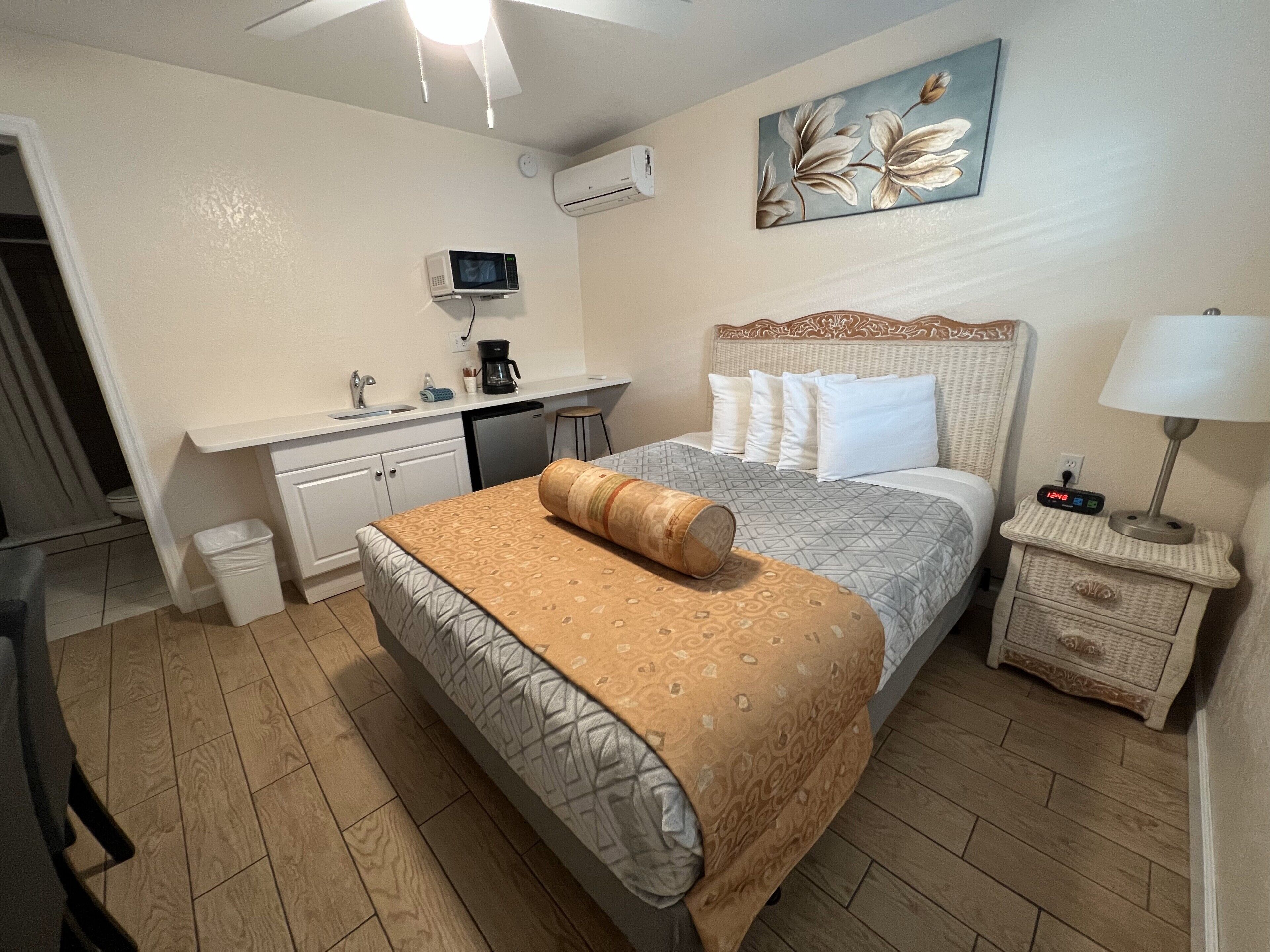 Quarto com cama, mesa de cabeceira, abajur e escrivaninha com cafeteira.