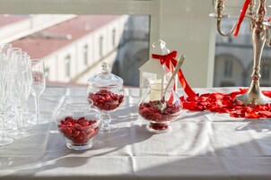 Uma mesa com recipientes de vidro transparente repletos de balas vermelhas, um castiçal branco com fita vermelha e um candelabro de prata.