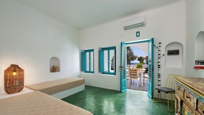 Quarto com piso verde, paredes brancas e portas azuis. Há uma cama, um banco e um armário de madeira com gavetas.