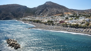 Uma cidade costeira com uma montanha ao fundo, uma praia com guarda-sóis e edifícios ao longo da costa.