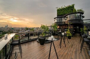 Um bar no terraço com mesas ao ar livre, vista para a cidade e estrutura de vidro curva.