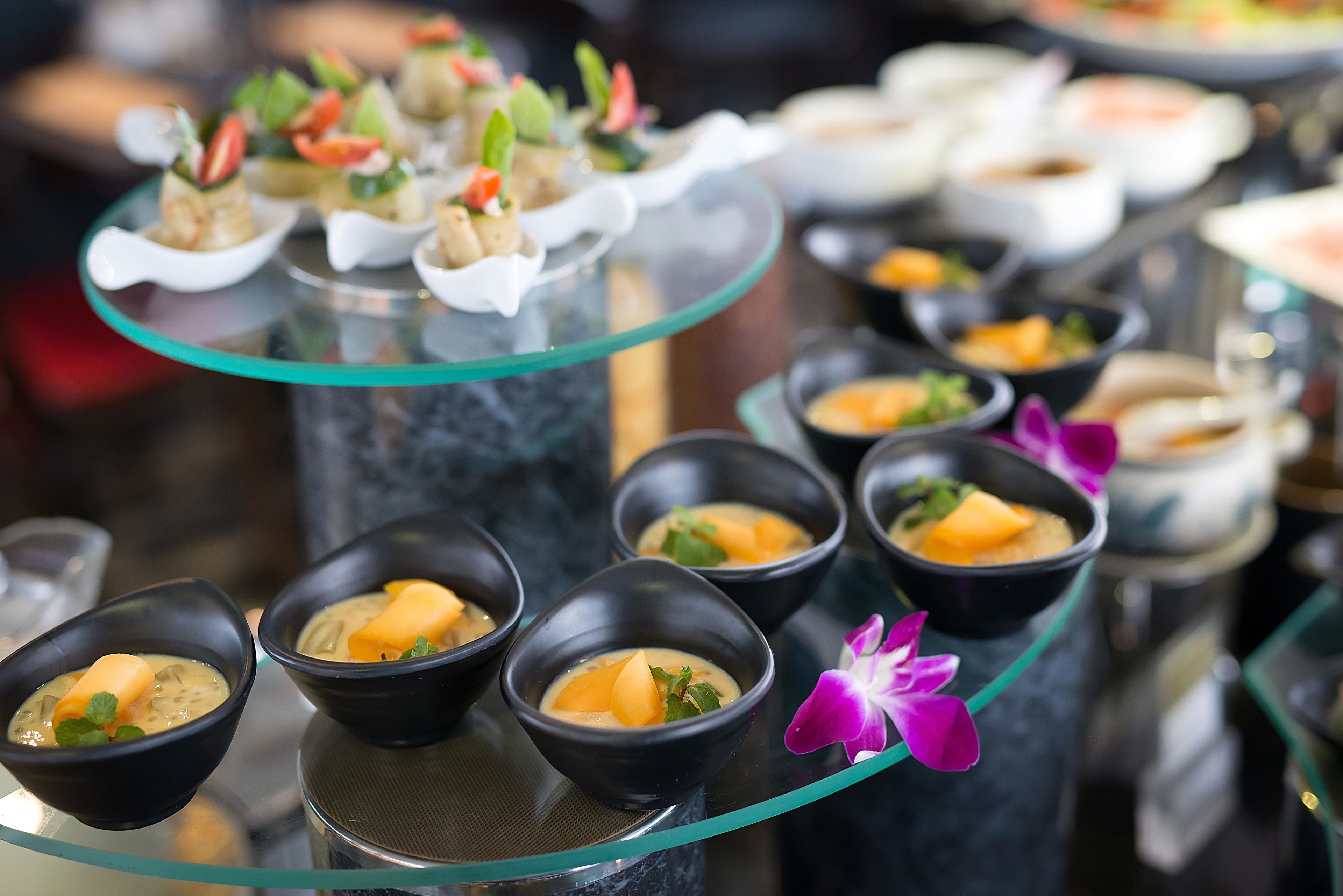 Diversos pratos em mesa de vidro, incluindo tigelas com o que parece ser sopa e outros pratos pequenos com aperitivos.