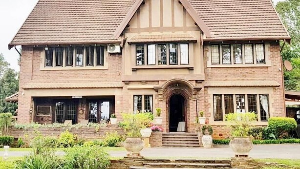 Uma casa de dois andares em tijolo com fachada simétrica, entrada central em arco e um pequeno jardim com uma fonte de pedra.