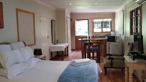 Quarto de hotel com cama, escrivaninha, cadeira, televisão e janela.