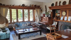 Uma sala de estar acolhedora com sofá, poltronas, mesa de centro e lareira. Há estantes e um relógio na parede.
